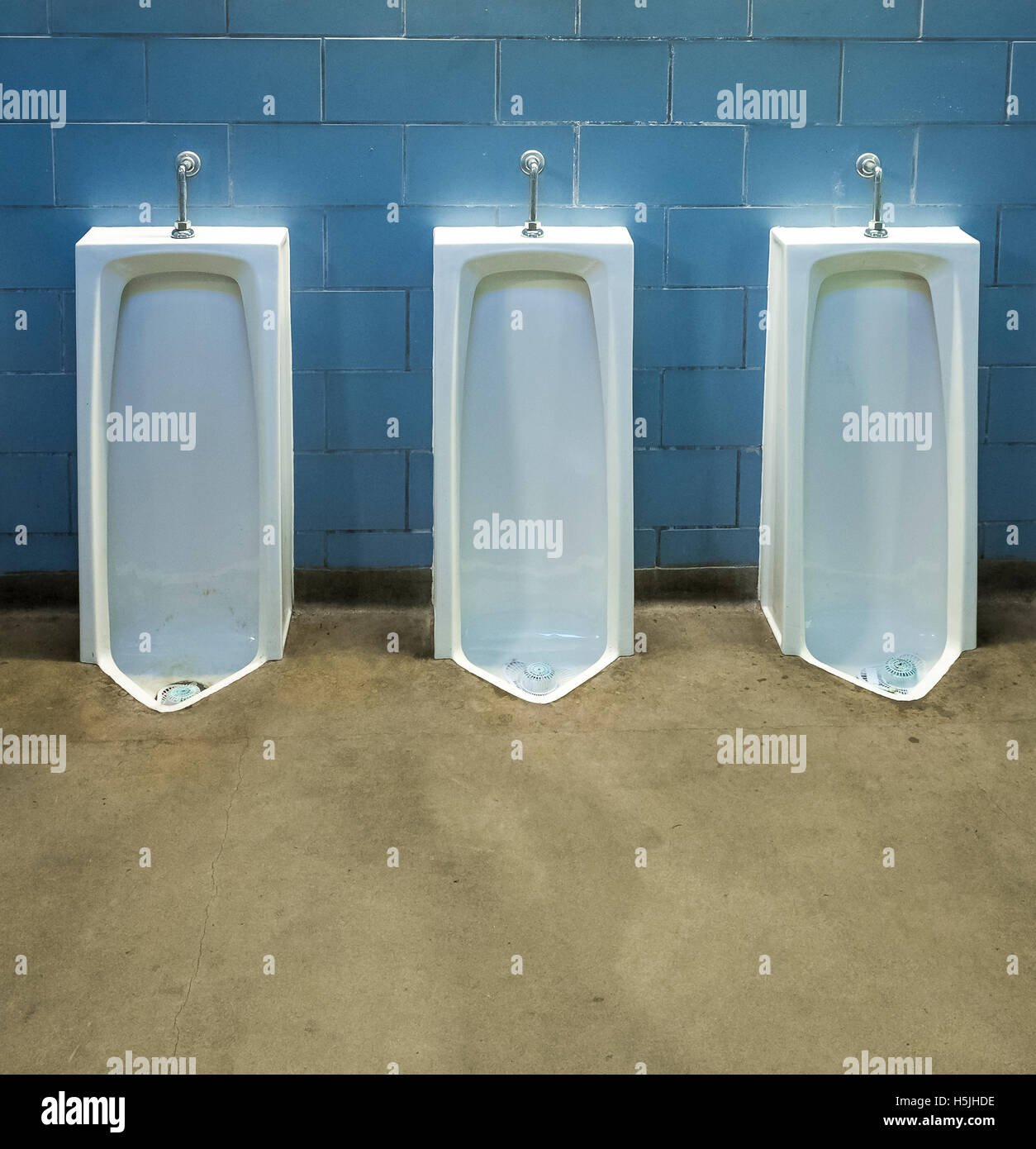 Three white urinals against a blue painted brick block wall Stock Photo ...