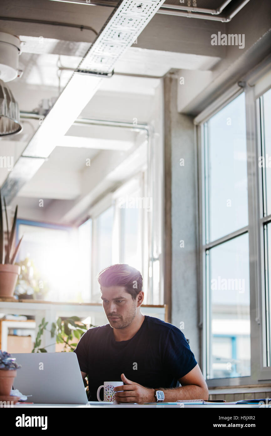 Vertical shot of young creative professional sitting at his desk with ...
