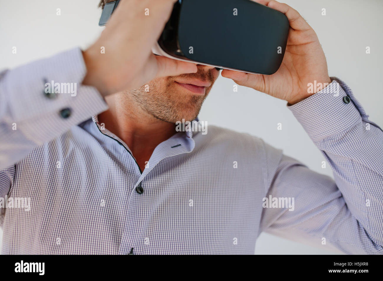 Shot of young man using the virtual reality headset against grey ...