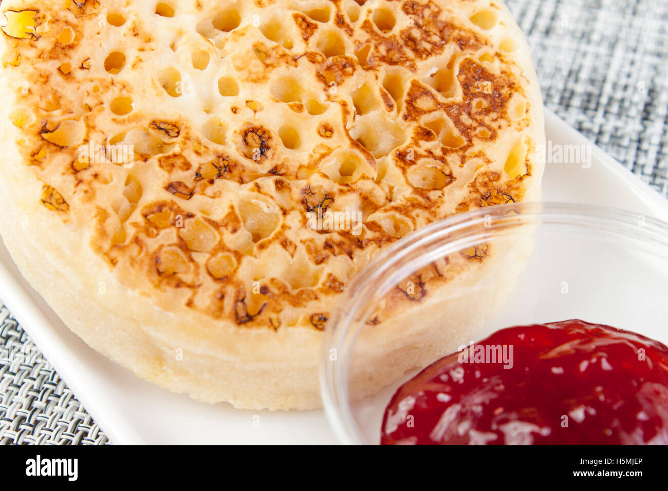 Close up shot of a plated golden crumpet with strawberry jam on a ...
