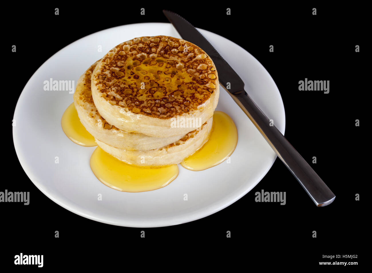 Pile of fresh crumpets in a puddle of golden maple syrup on a white ...