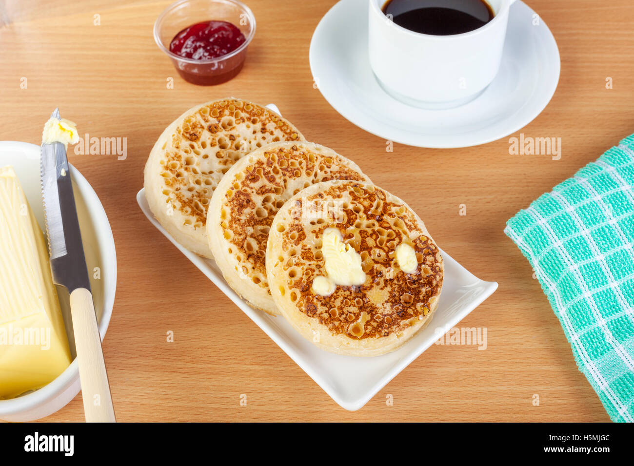 Rectangular plate of butter drenched crumpets and black coffee on a ...