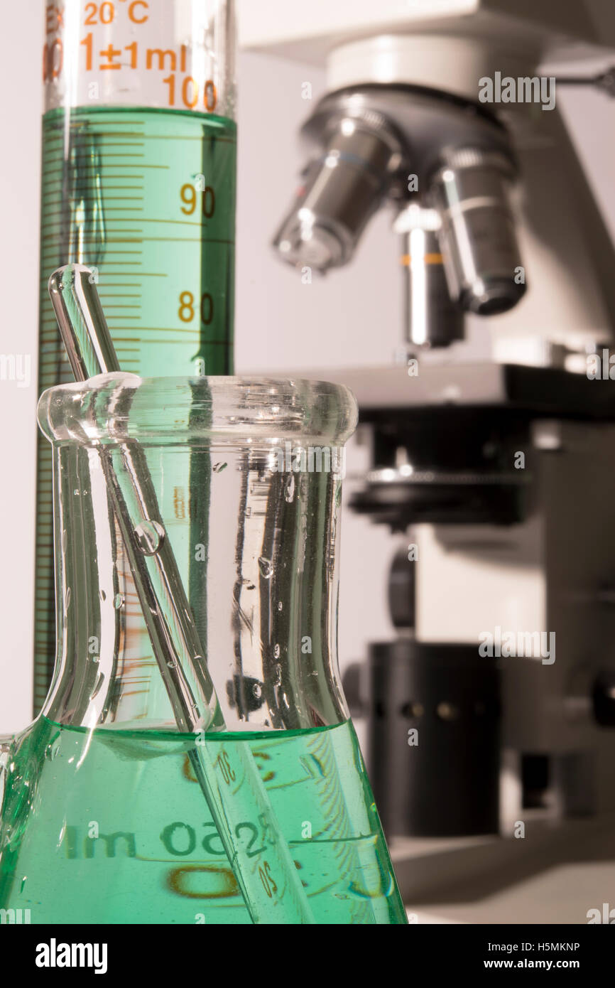 closeup of chemistry flask, graduated cylinder with microscope in ...