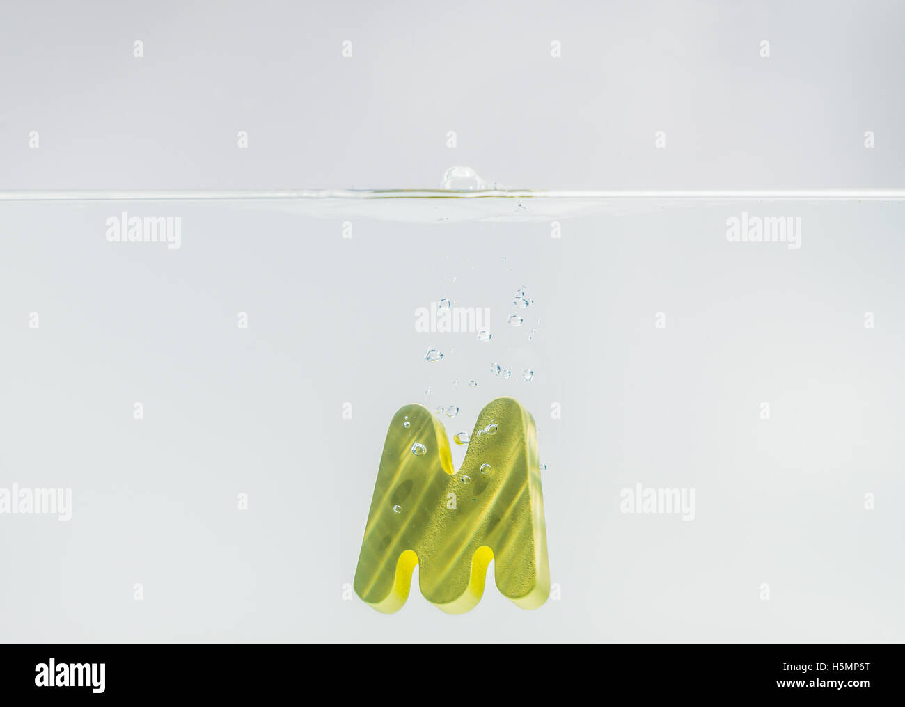 Yellow wooden alphabet M drop in the water with white background and ...