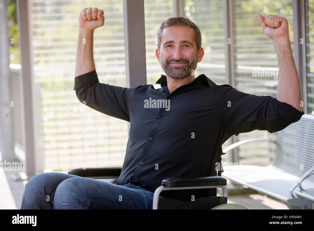 handsome man in wheelchair lifting his arms and looking very optimistic ...