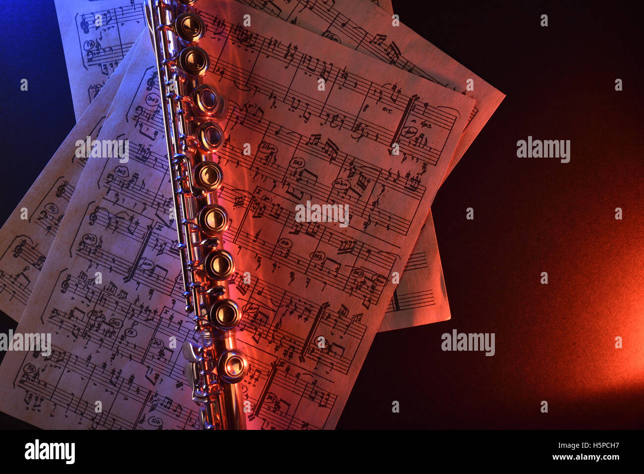 Transverse flute and old sheet music on black table red blue ...