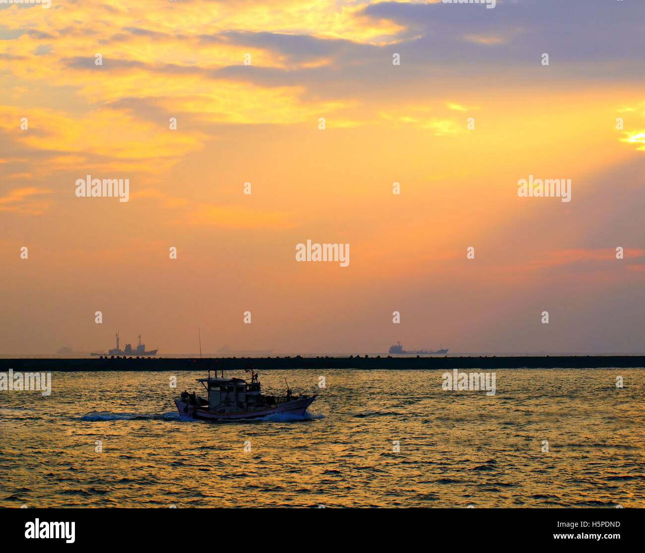 A small fishing vessel heads out to sea at sunset Stock Photo - Alamy