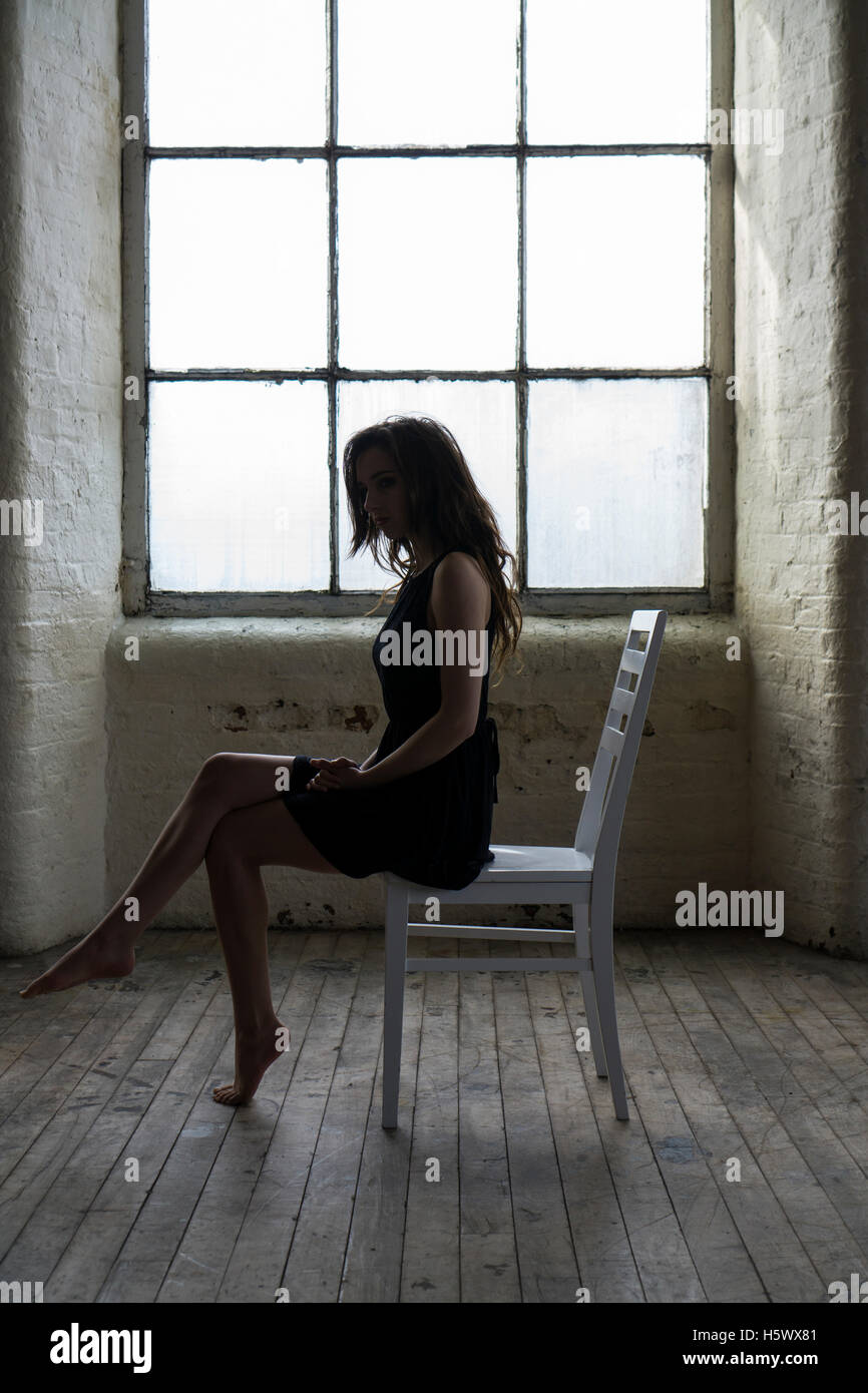 Sad woman sat on a chair by the window Stock Photo - Alamy