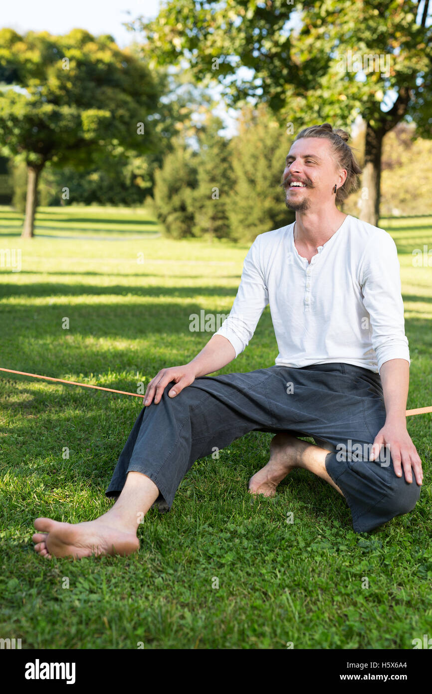 Portrait of man sitting on slackline and resting Stock Photo - Alamy