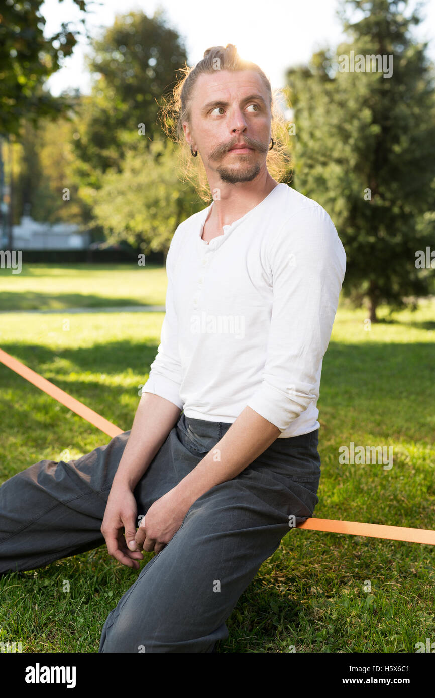 Man sitting on tightrope or slackline concentrating to keep balance ...