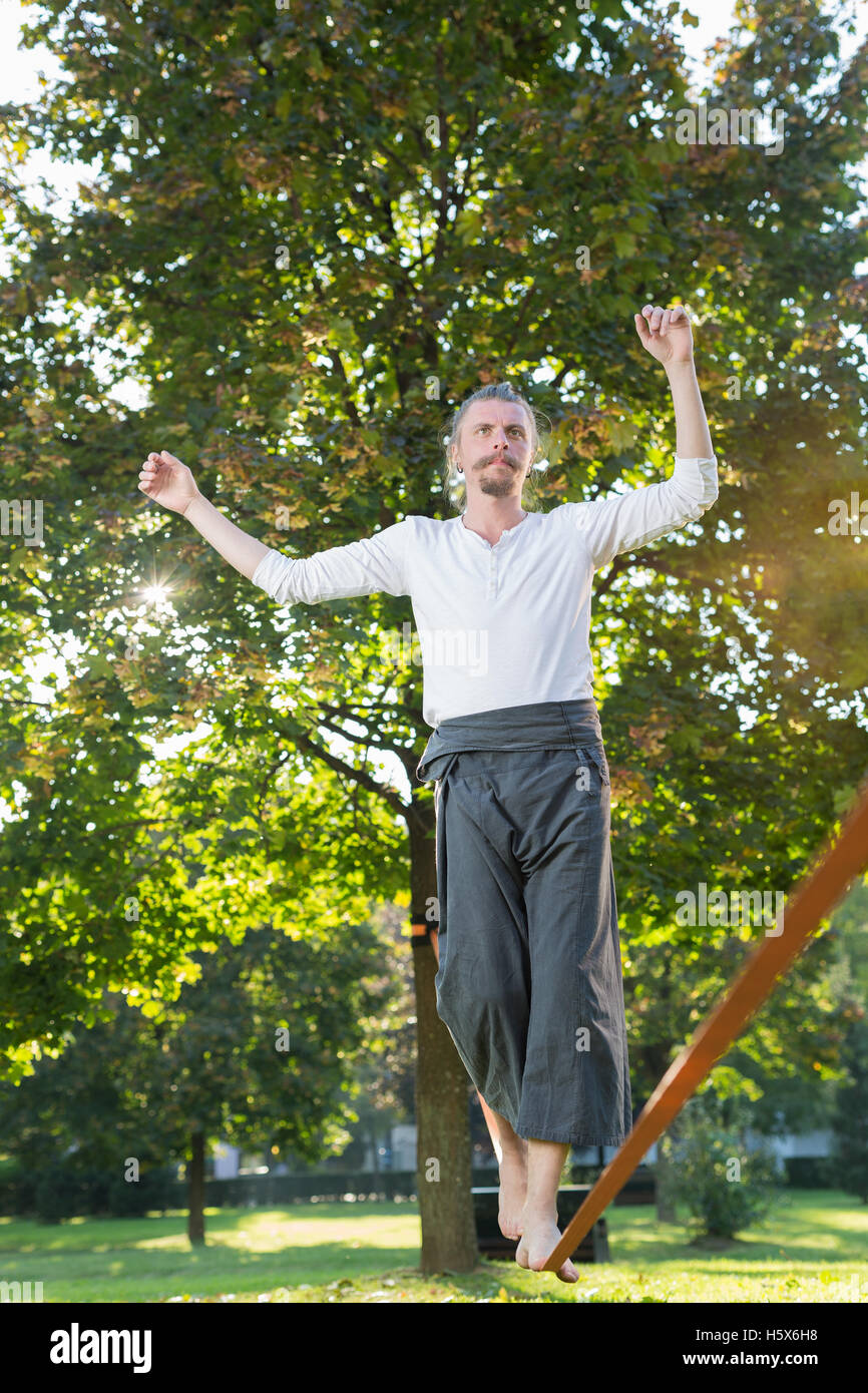 Man walking barefoot on slackline in park with arms out Stock Photo - Alamy