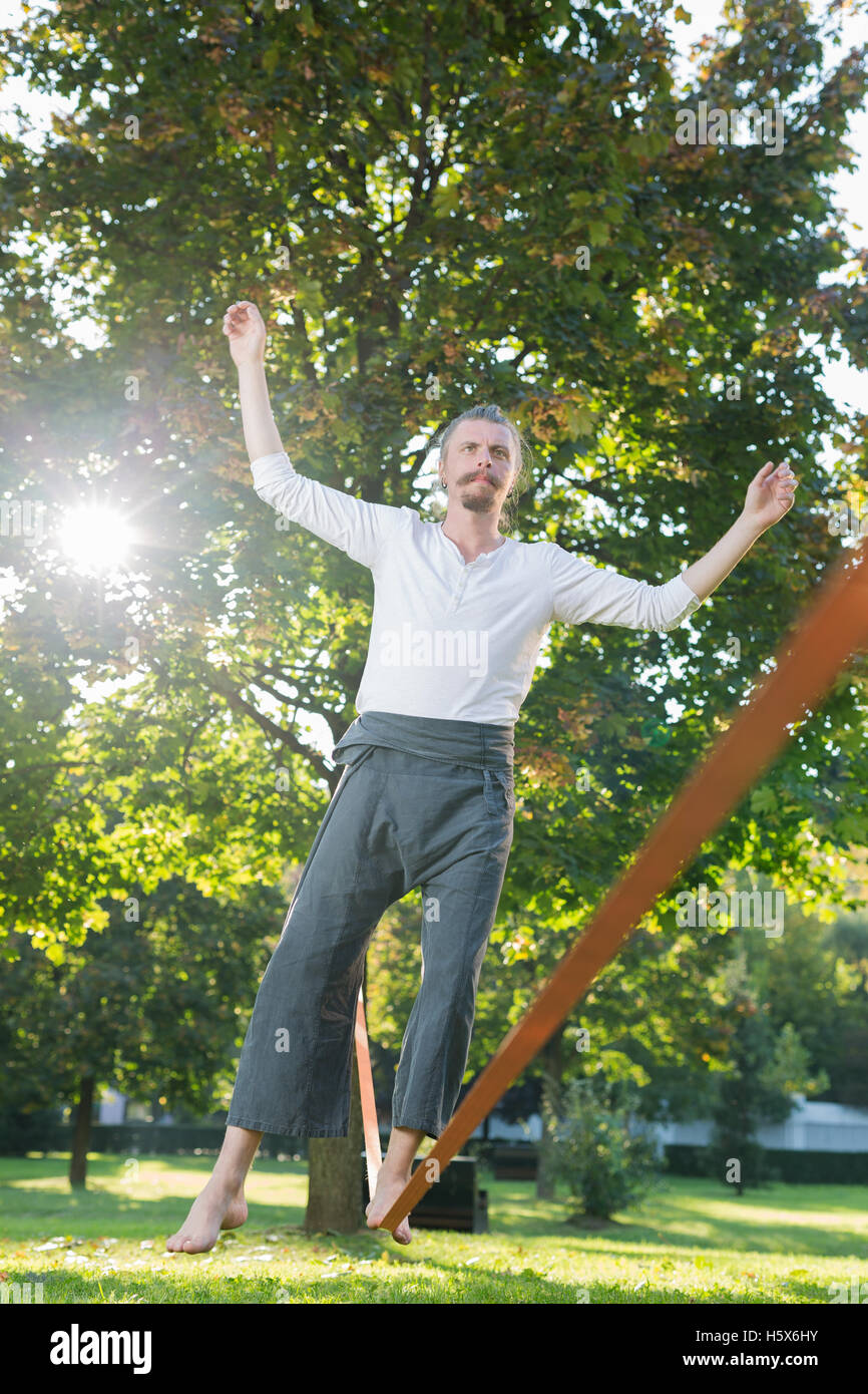 Portrait of man balancing a tightrope or slackline in park environment ...