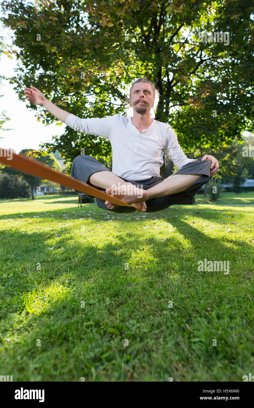 Man sitting on tightrope or slackline concentrating to keep balance ...