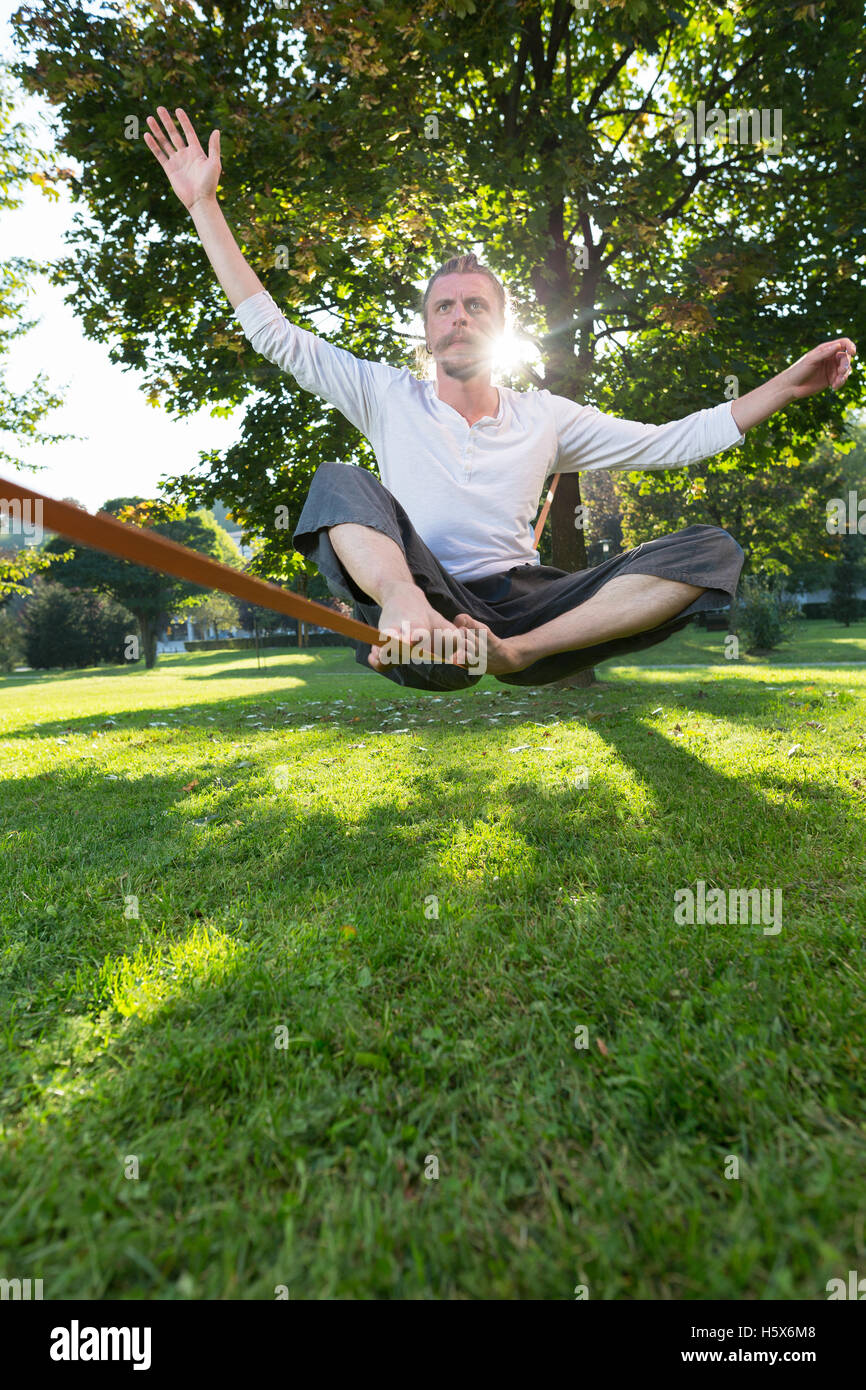 Man sitting on tightrope or slackline concentrating to keep balance ...