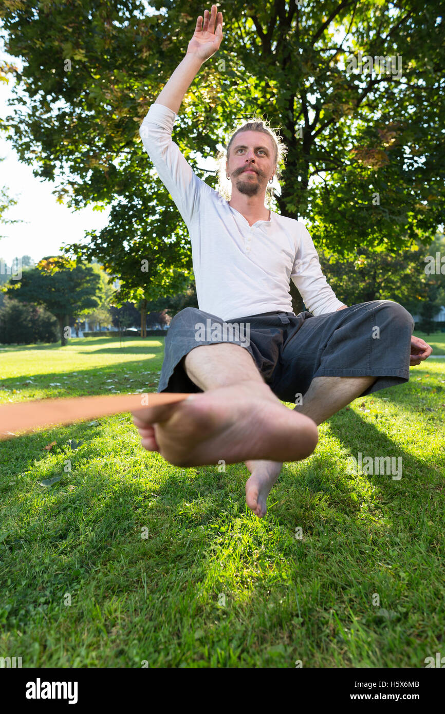Man sitting on tightrope or slackline concentrating to keep balance ...
