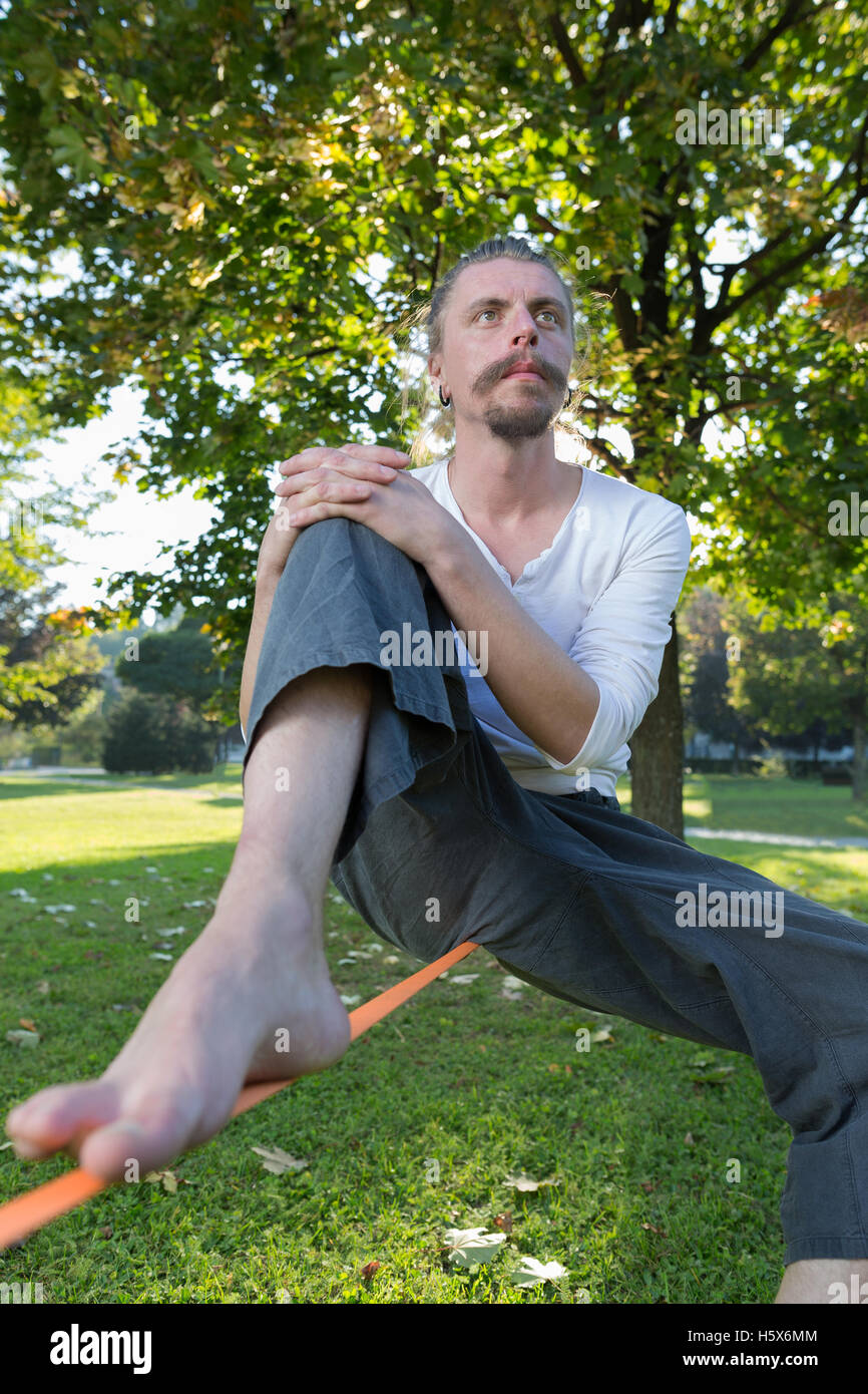 Portrait of man sitting on slackline and resting Stock Photo - Alamy