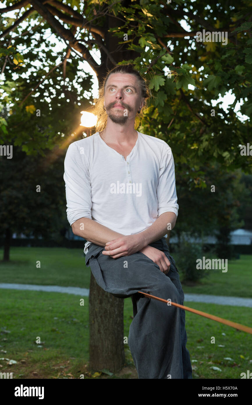 Portrait of man sitting on slackline and resting Stock Photo - Alamy