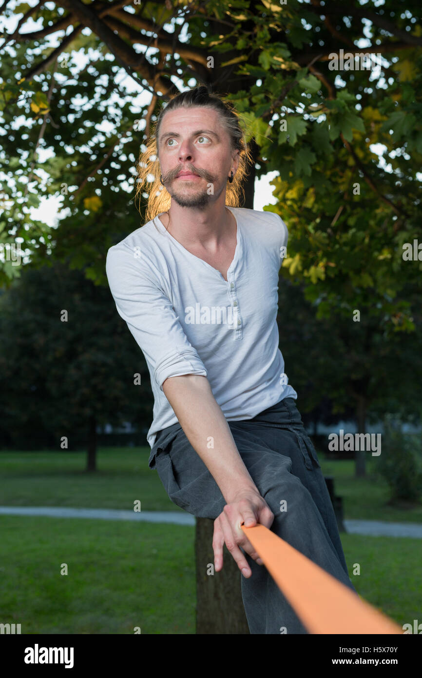 Portrait of man sitting on slackline and resting Stock Photo - Alamy