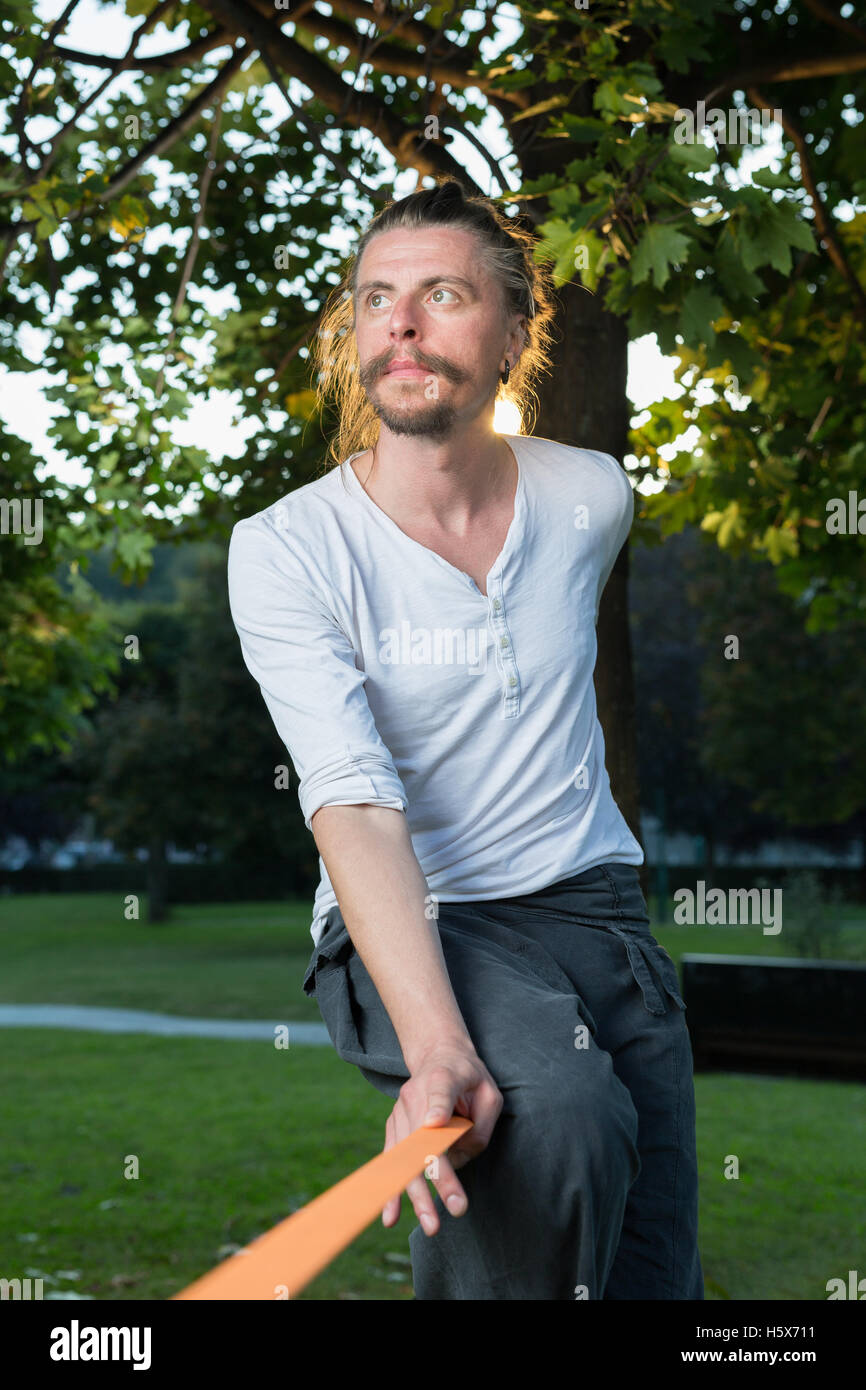 Portrait of man sitting on slackline and resting Stock Photo - Alamy
