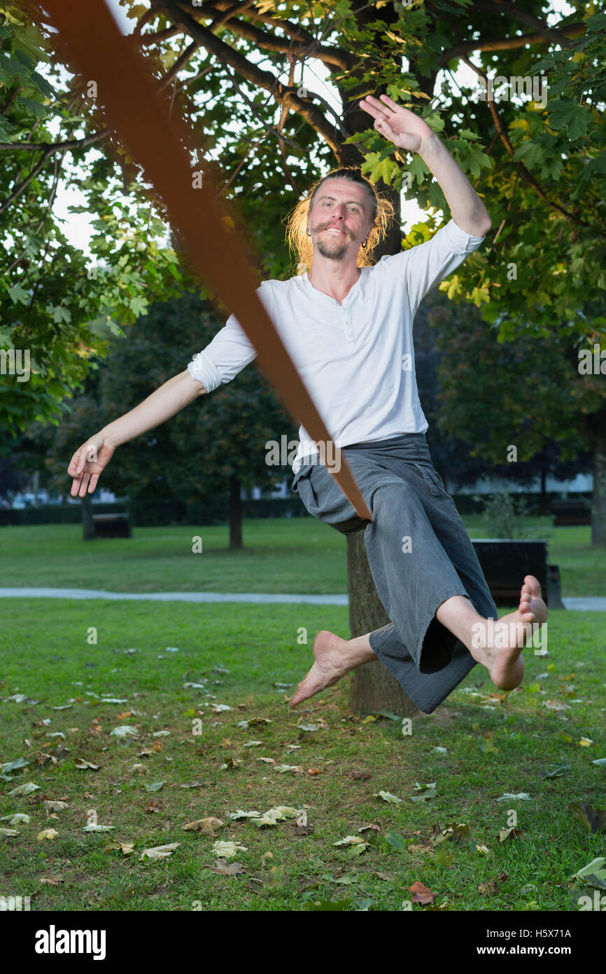 Man sitting on tightrope or slackline concentrating to keep balance ...