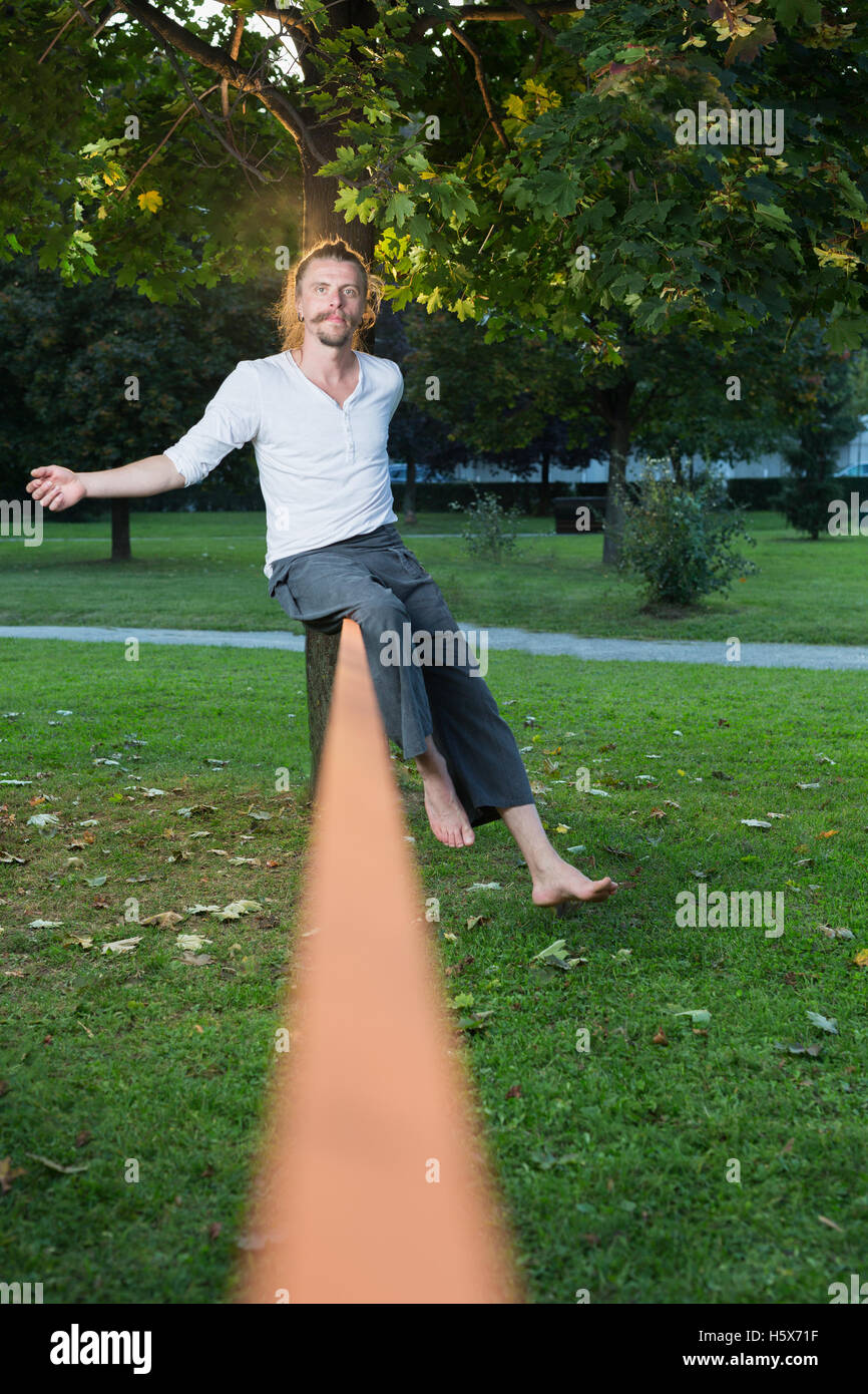 Man sitting on tightrope or slackline concentrating to keep balance ...