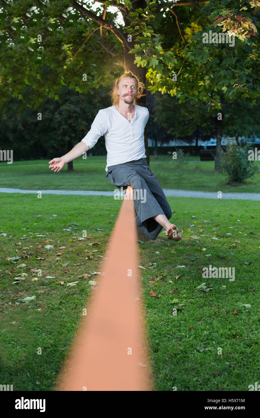 Portrait of man sitting on slackline and resting Stock Photo - Alamy