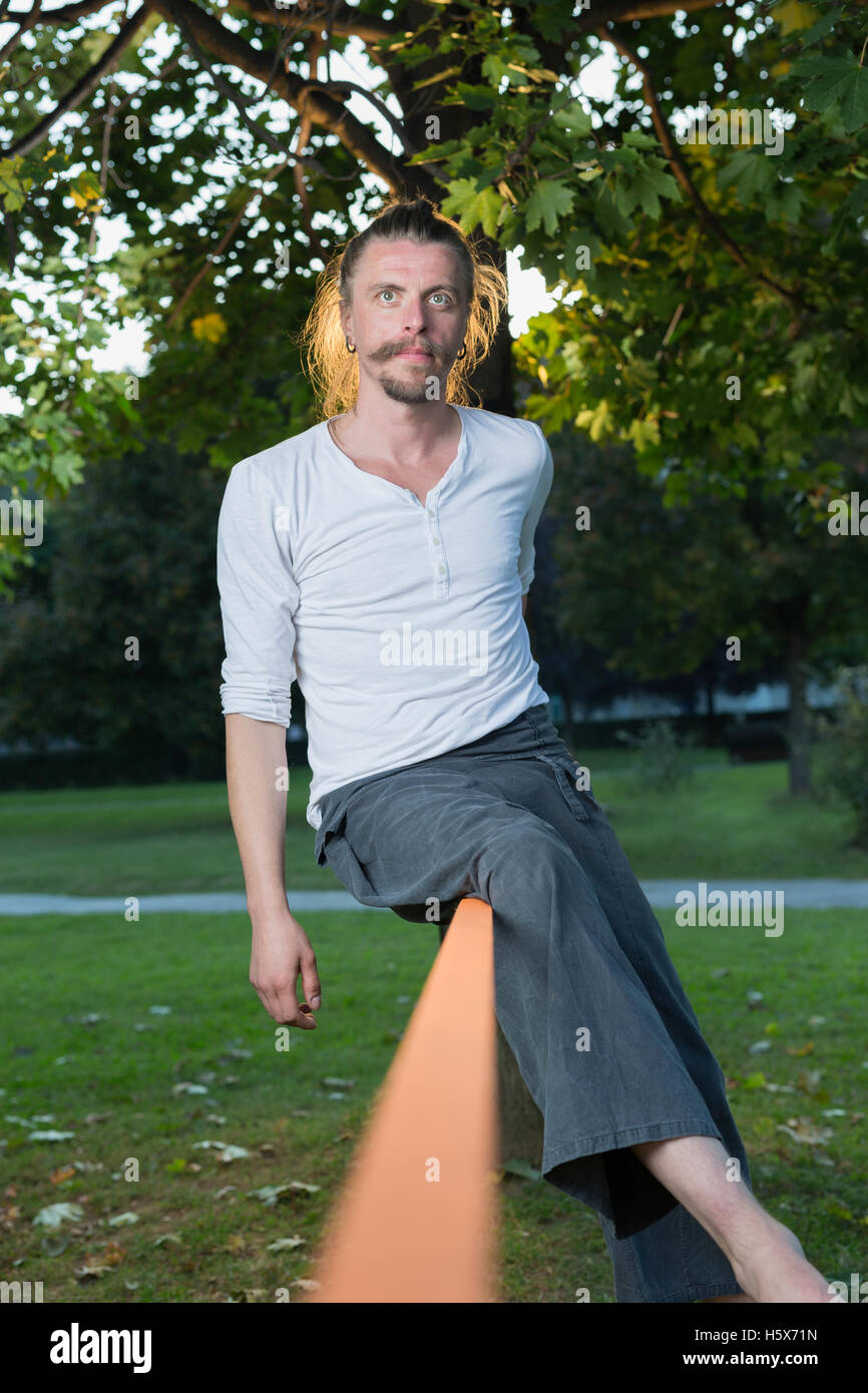 Portrait of man sitting on slackline and resting Stock Photo - Alamy