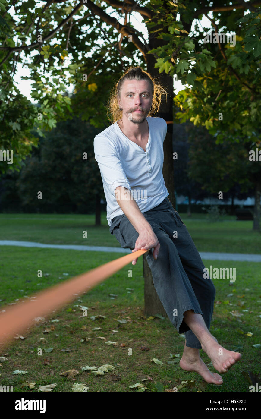 Portrait of man sitting on slackline and resting Stock Photo - Alamy