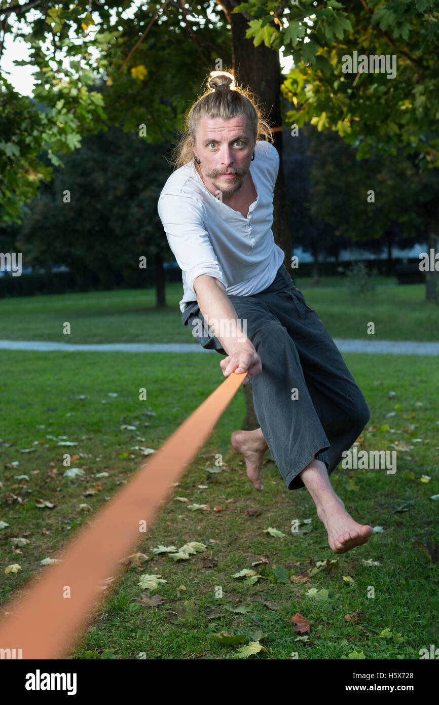 Man sitting on tightrope or slackline concentrating to keep balance ...