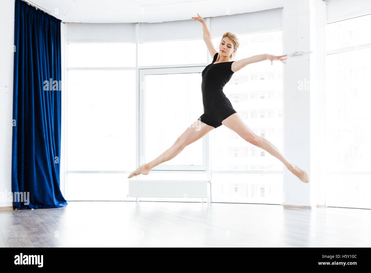 Graceful young woman ballerina dancing and jumping in ballet studio ...