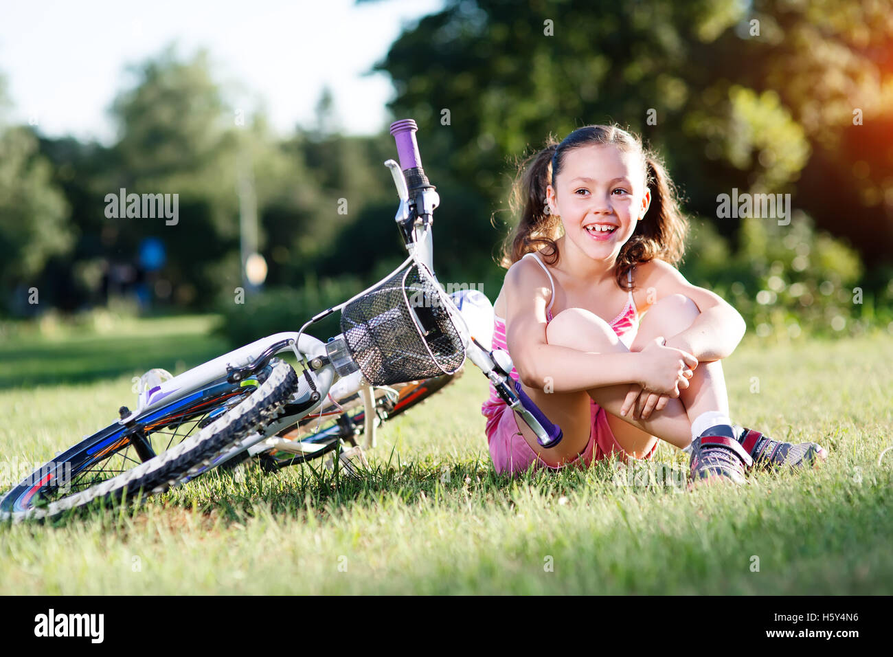 Portrait of girl with bicycle. Little girl sitting on grass in the park ...