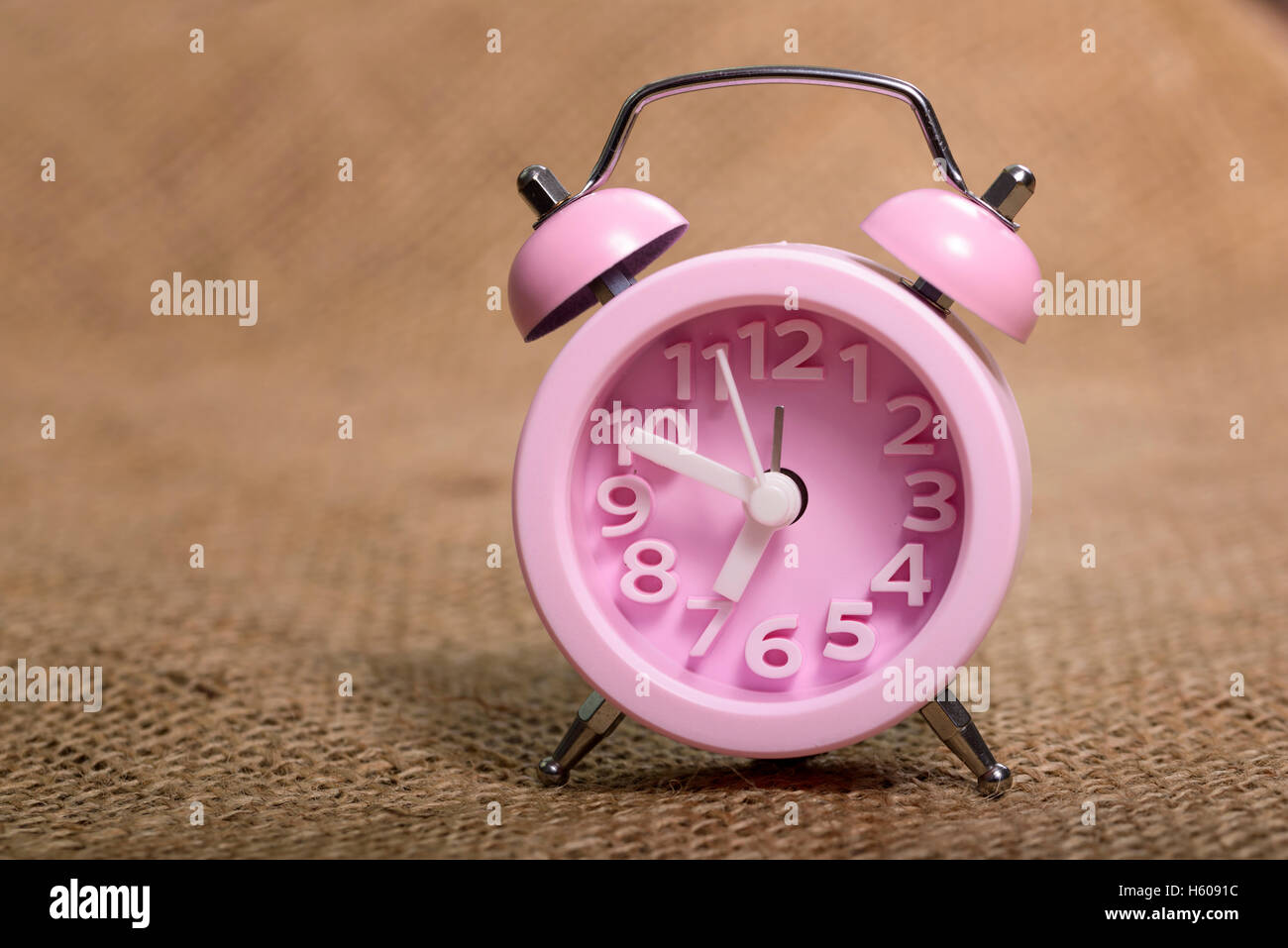 Clock Alarm set at ten to seven on jute background Stock Photo - Alamy