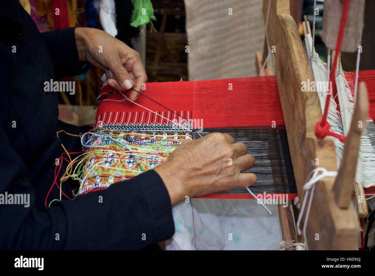 Old woman weaving red black and multi color cotton flag pattern on loom ...