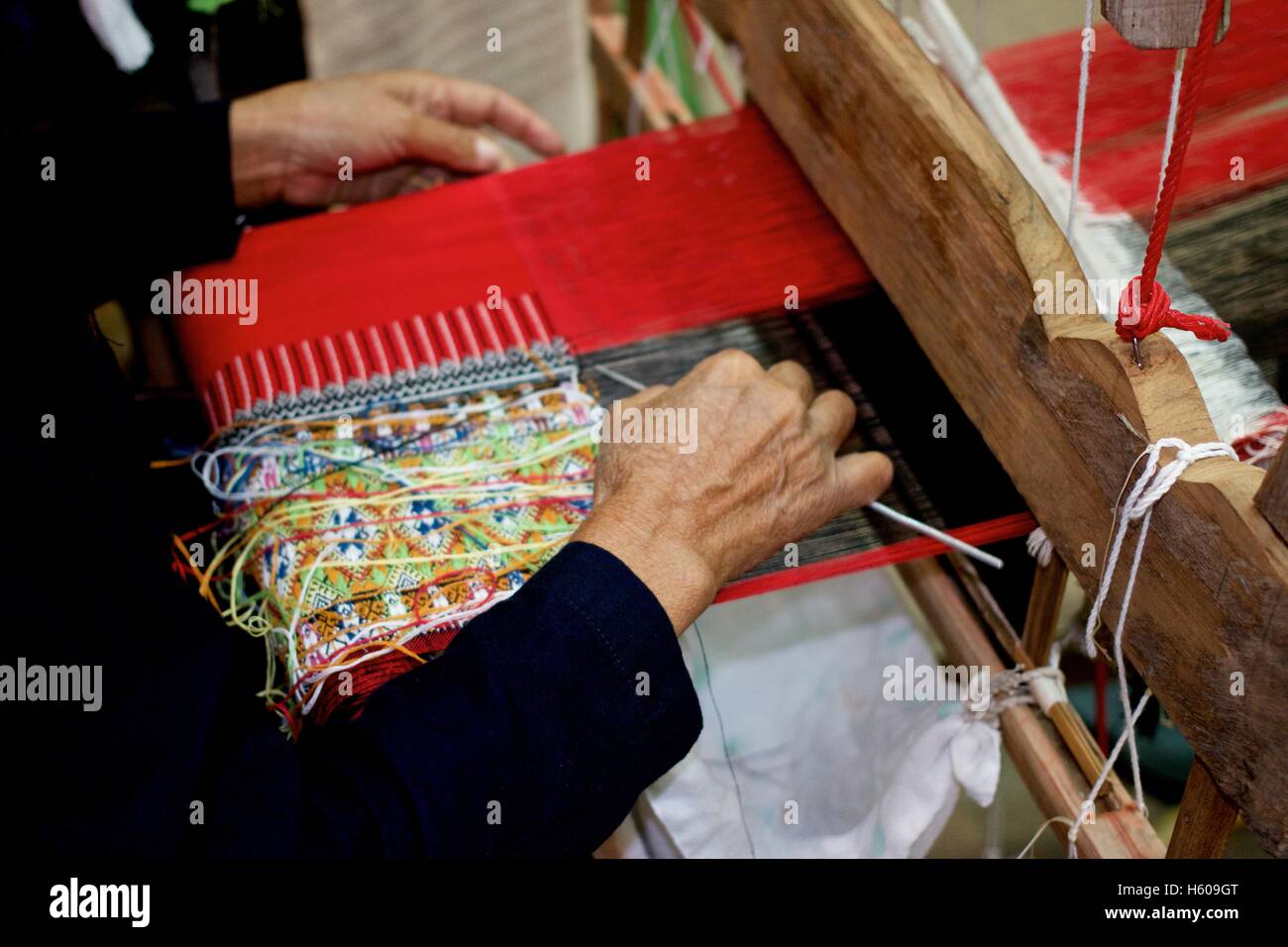 Old woman weaving red black and multi color cotton flag pattern on loom ...