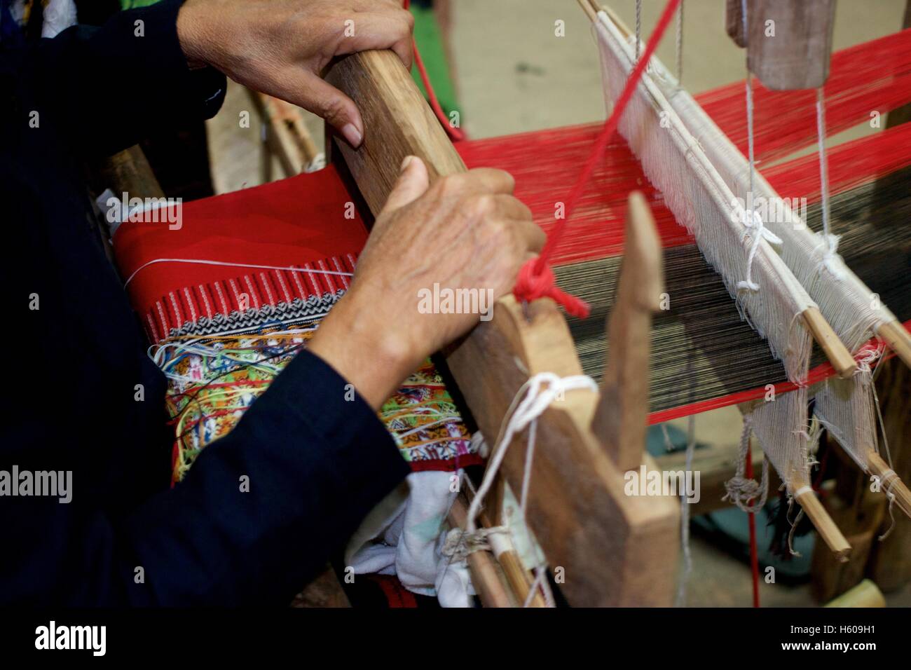 Old woman weaving red black and multi color cotton flag pattern on loom ...