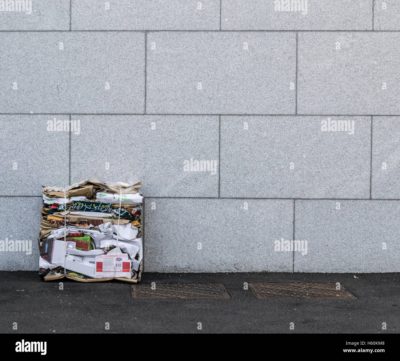Flattened paper and cardboard recycling sits against a grey stone wall ...