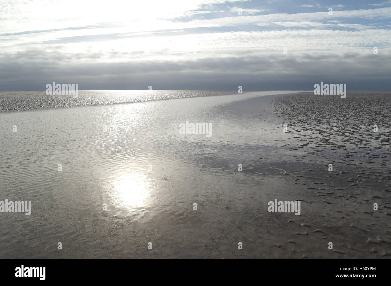 Grey clouds beach view with white sun disk reflecting in shallow sea ...