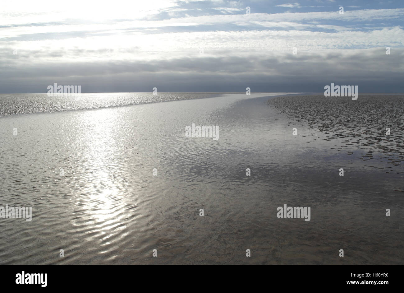 Grey clouds sky with white sun disk reflecting in ripples of sea water ...