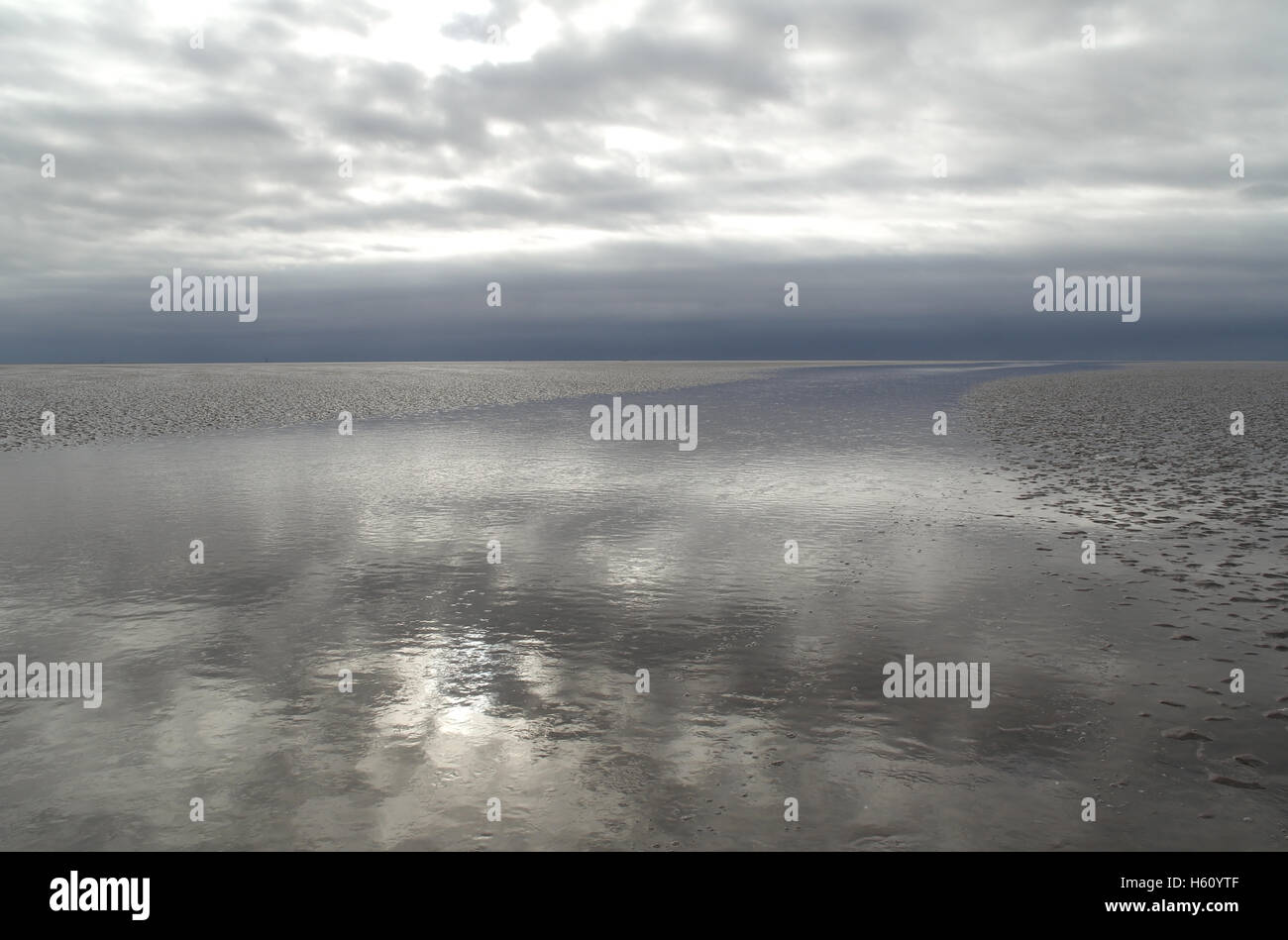 Grey clouds sky with white sun openings reflecting in sea water channel ...