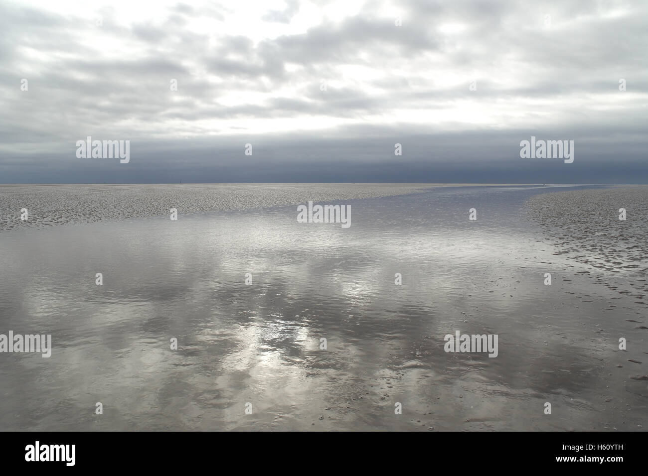 Grey clouds sky with white sun openings reflecting in sea water channel ...