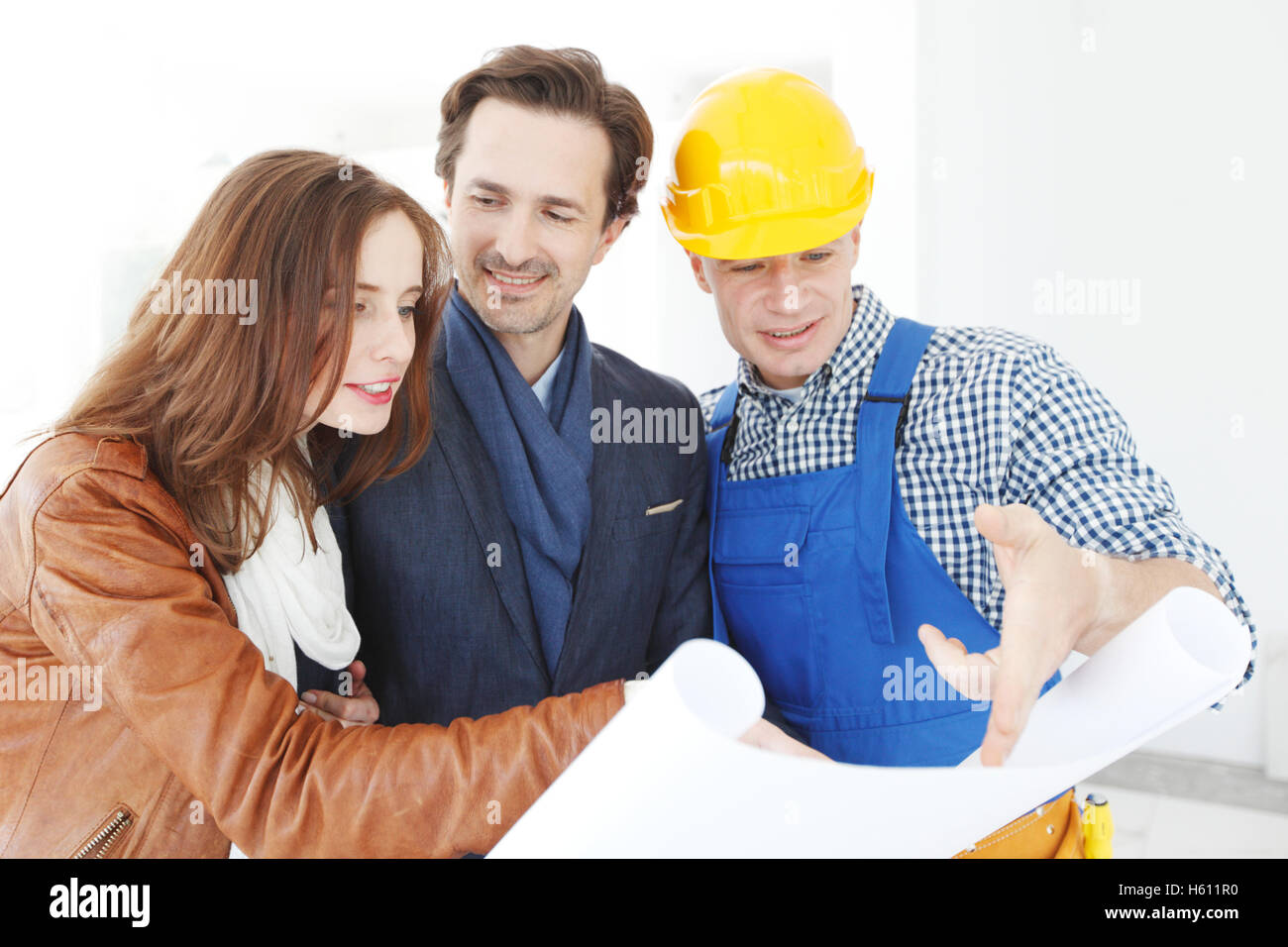 Worker shows house design plans to a young couple at construction site ...