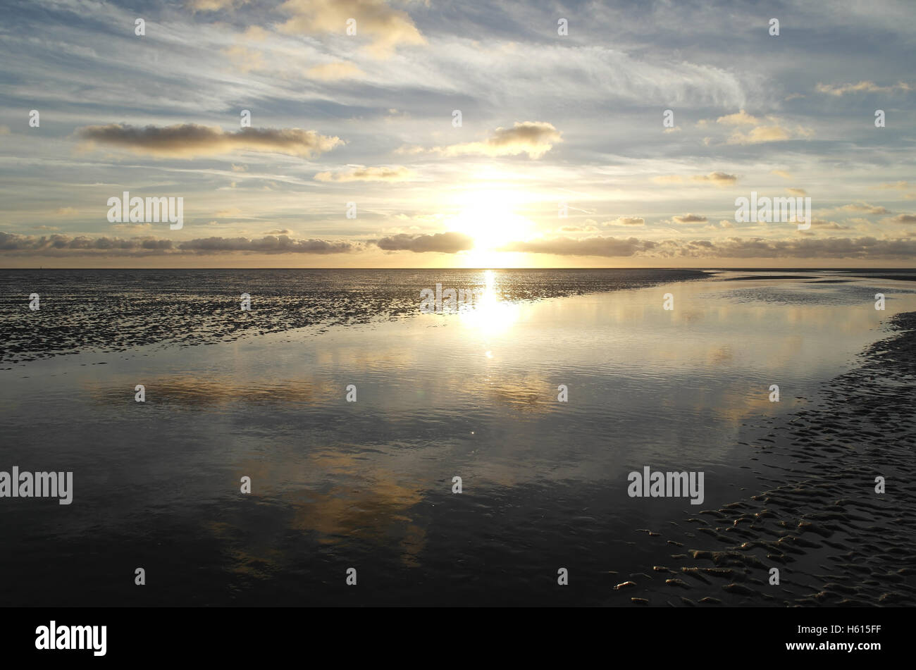 White sun setting below small grey stratocumulus clouds reflecting in a ...