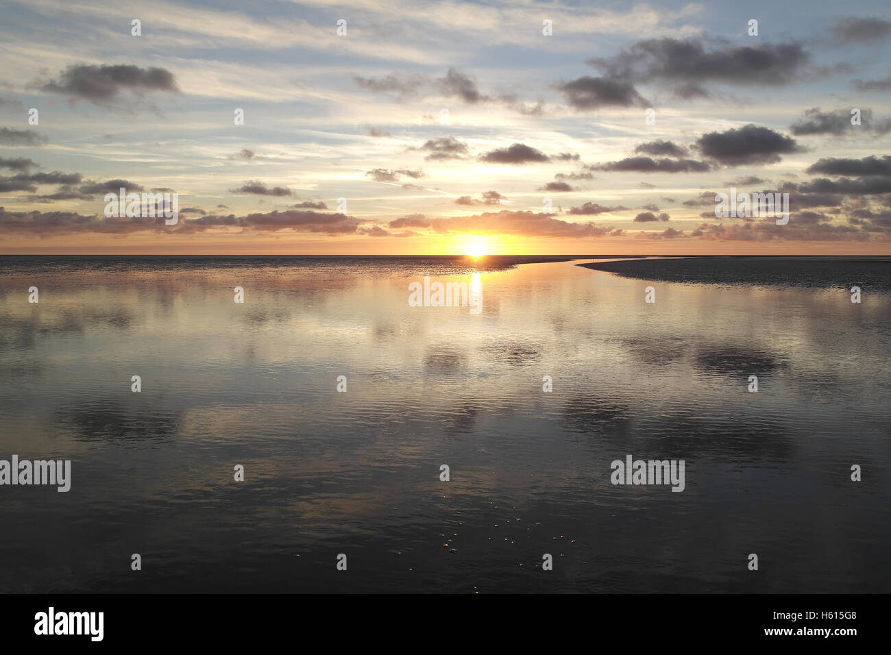 Grey stratocumulus clouds reflecting in sea water channel crossing sand ...