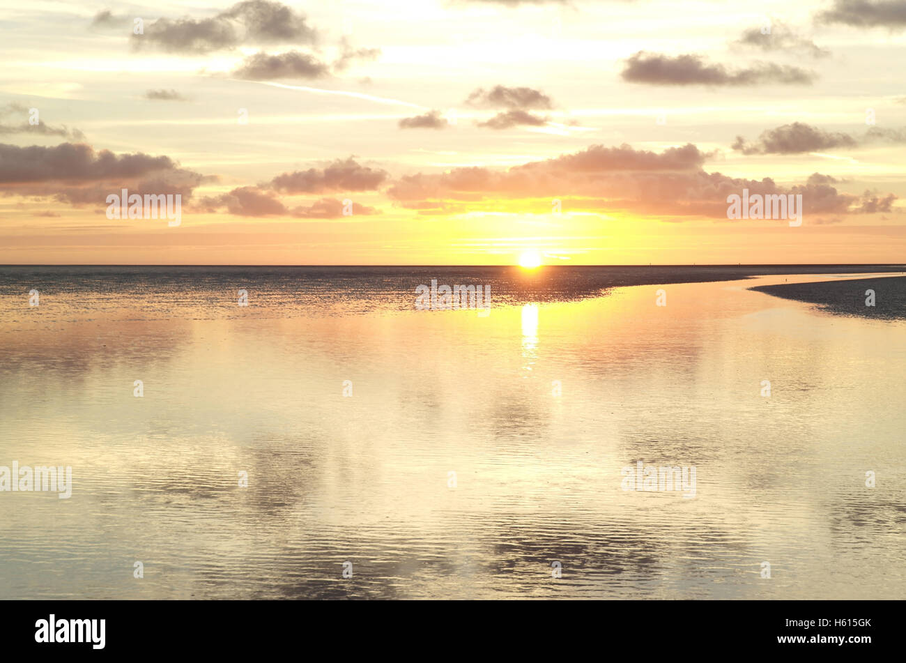 View across expanse of beach sand with water channel to yellow sun ...