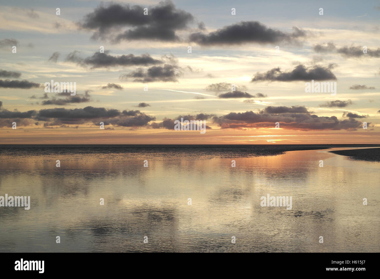 Many dark grey stratocumulus clouds reflecting in sand beach sea water ...