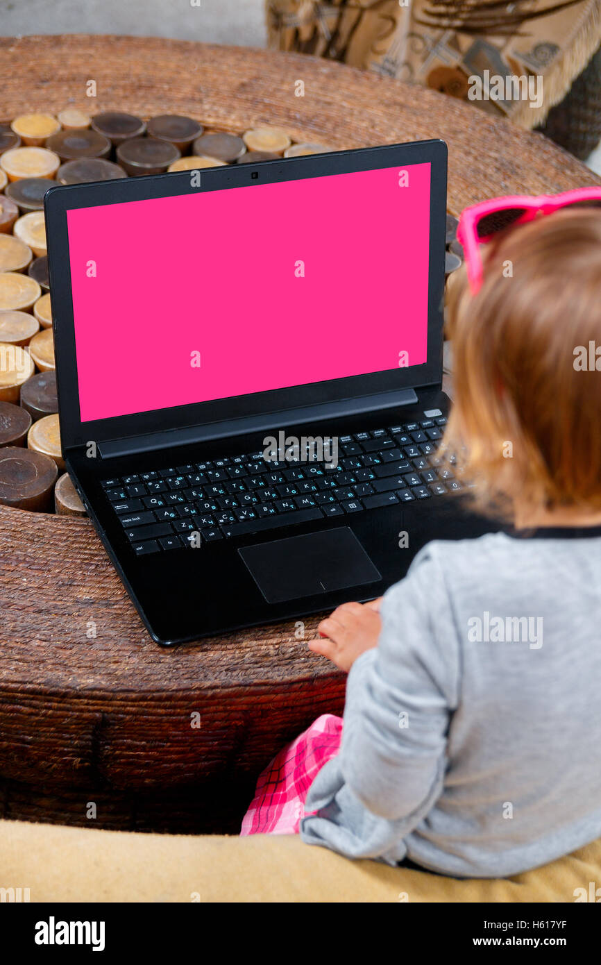 Little girl using laptop. Unrecognized child in pink skirt and pink ...