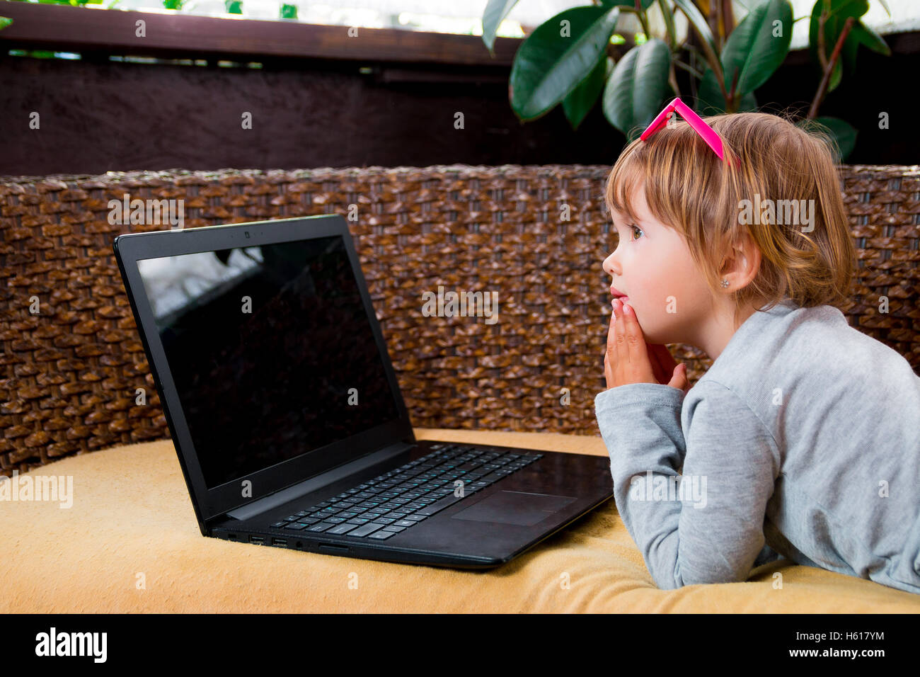Little girl using laptop. Child in pink sunglasses, grey top lying at ...