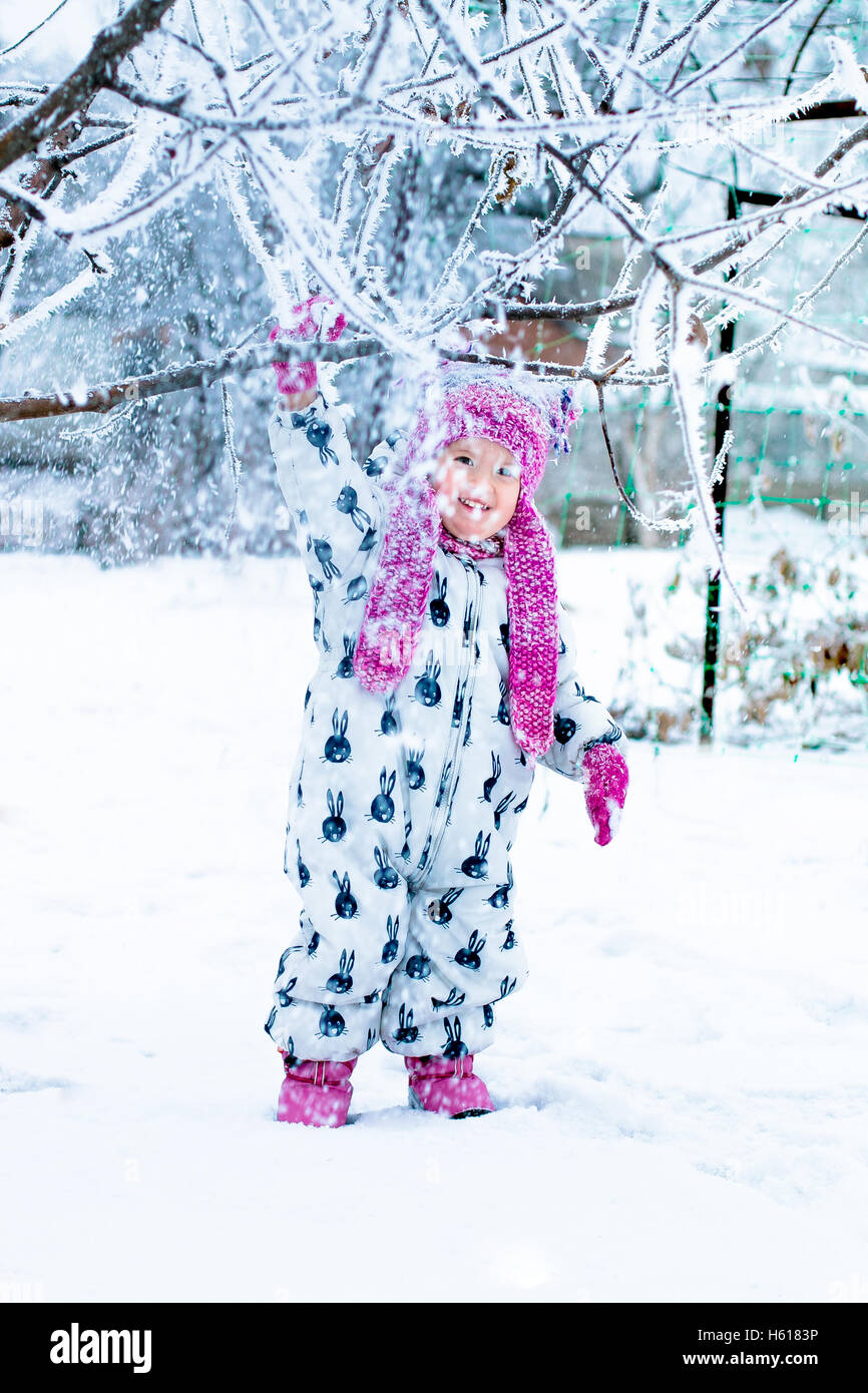 Child in snowy day. Snow falls from the tree. Baby girl in white ...