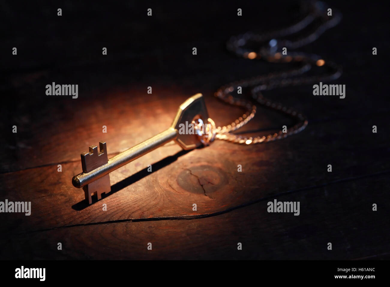 Key with chain on wooden background under beam of light Stock Photo - Alamy