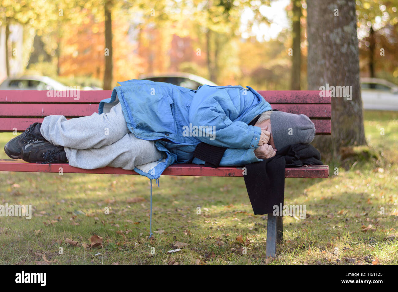 Homeless elderly woman sleeping rough in a park curled up against the ...